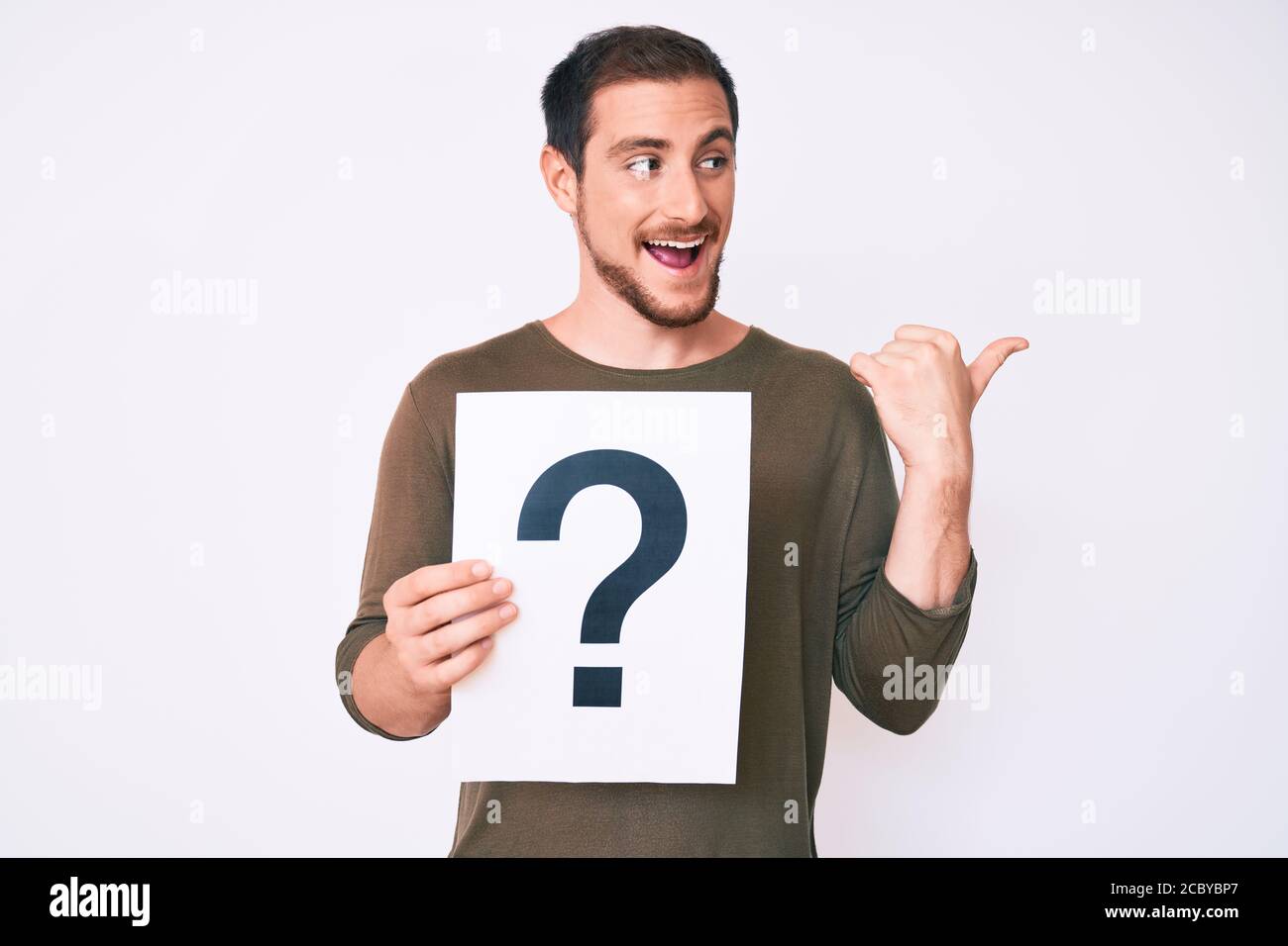 Young handsome man holding question mark pointing thumb up to the side ...