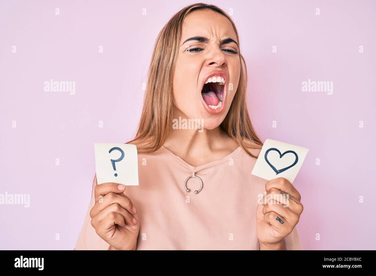 Young beautiful blonde woman holding heart and question mark reminder ...