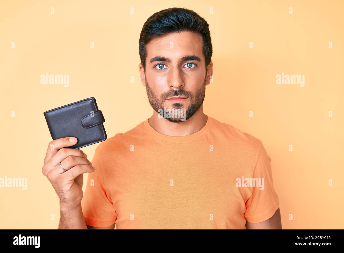 Young hispanic man holding leather wallet thinking attitude and sober ...