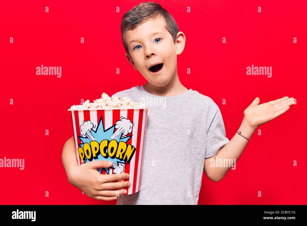 Cute blond kid holding popcorn celebrating achievement with happy smile ...