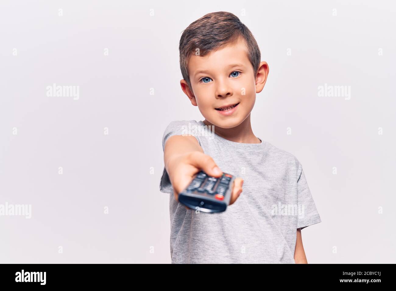 Cute blond kid holding television remote control looking positive and ...