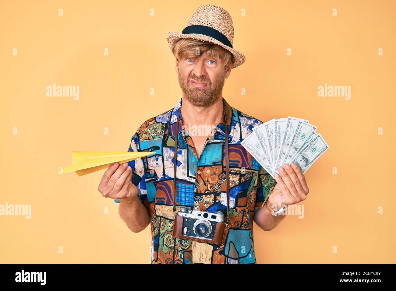 Young blond man wearing summer style holding paper plane and dollars ...