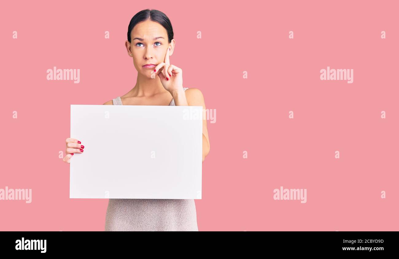 Beautiful brunette young woman holding blank empty banner serious face ...
