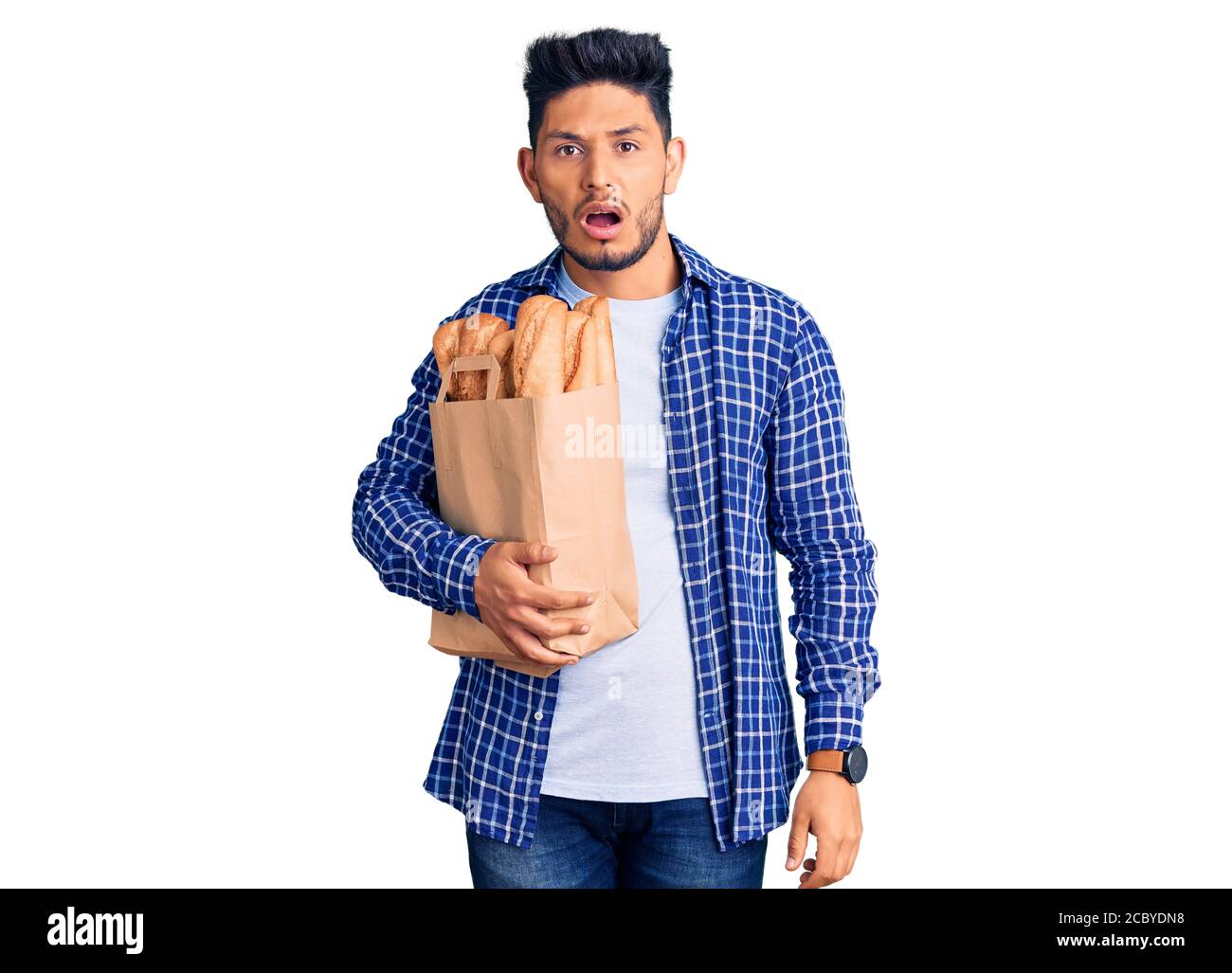 Handsome latin american young man holding paper bag with bread in shock ...