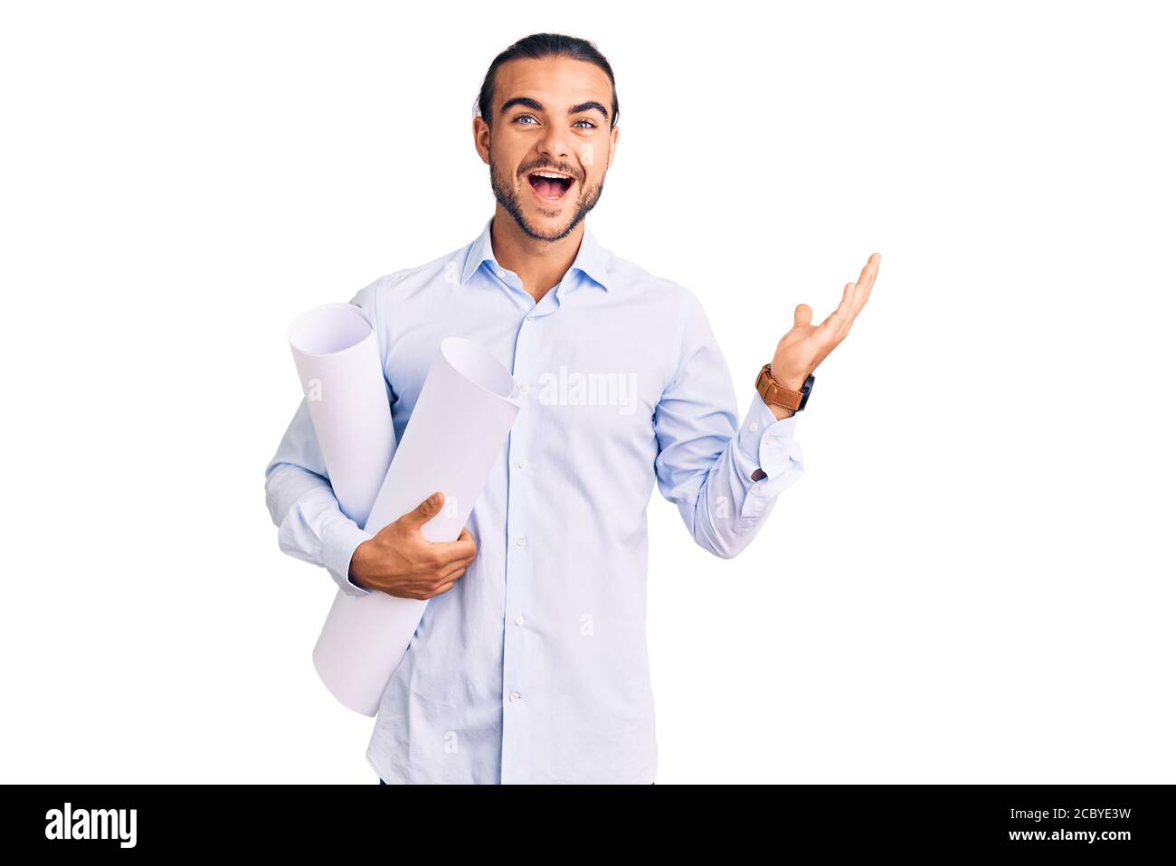 Young handsome man holding paper blueprints celebrating victory with ...