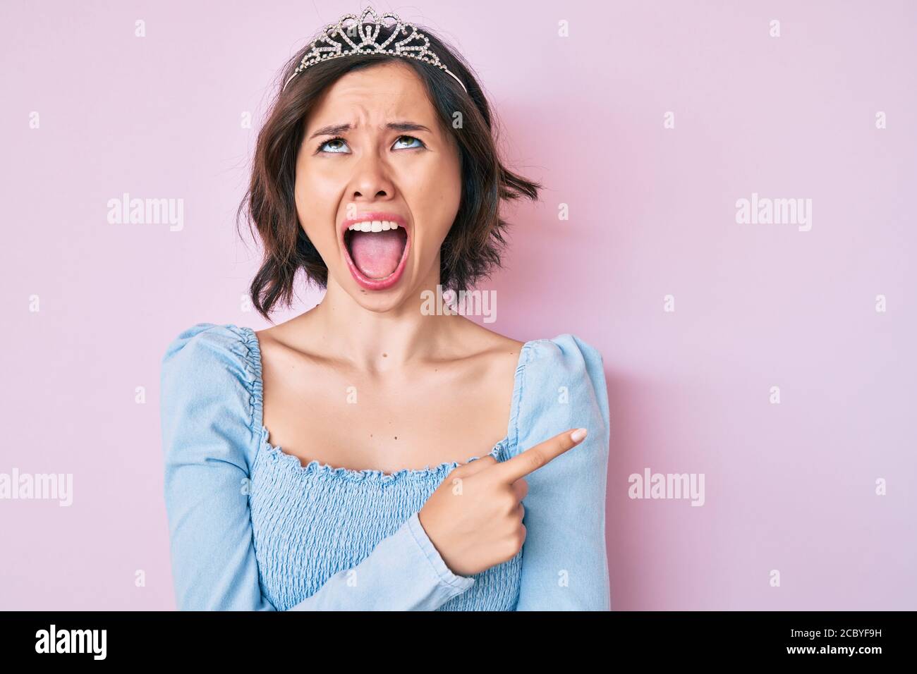 Young beautiful girl wearing princess crown angry and mad screaming ...