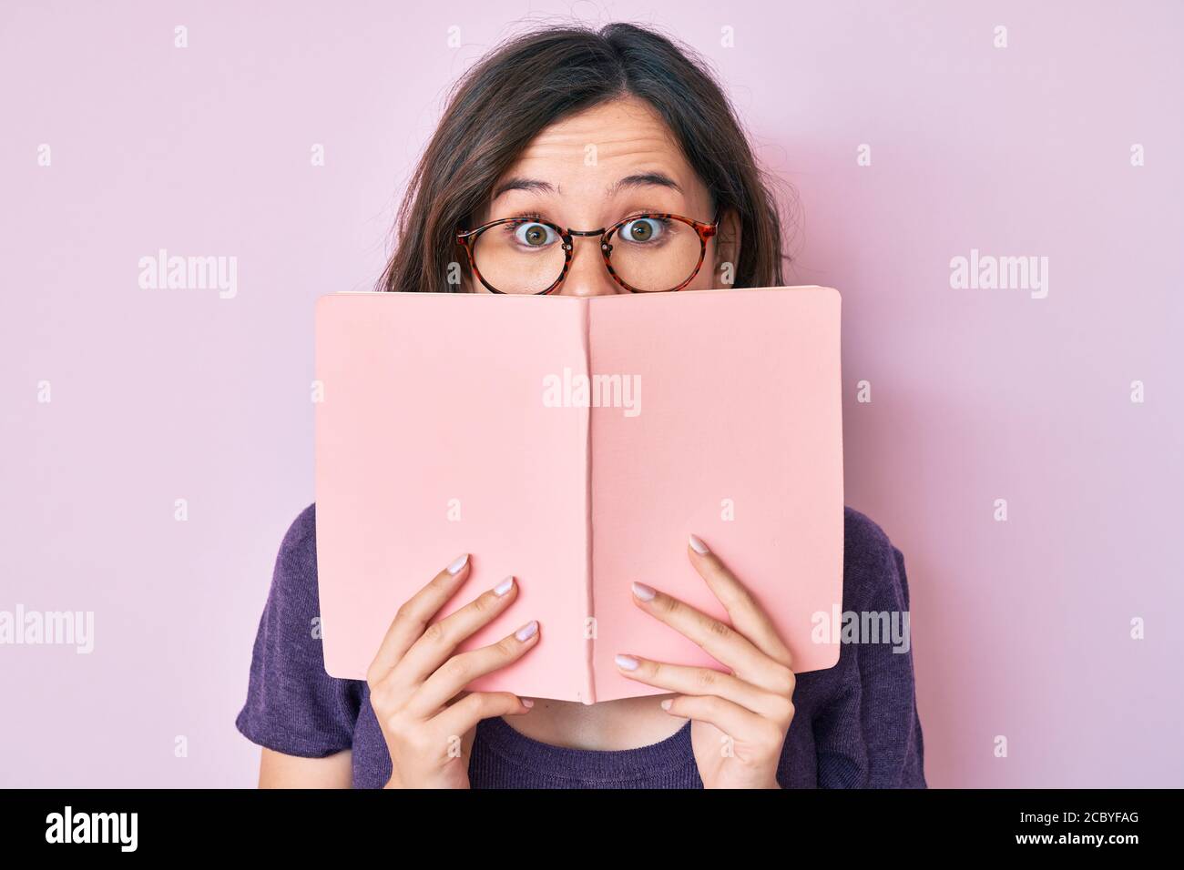 Young beautiful woman wearing glasses reading book afraid and shocked ...
