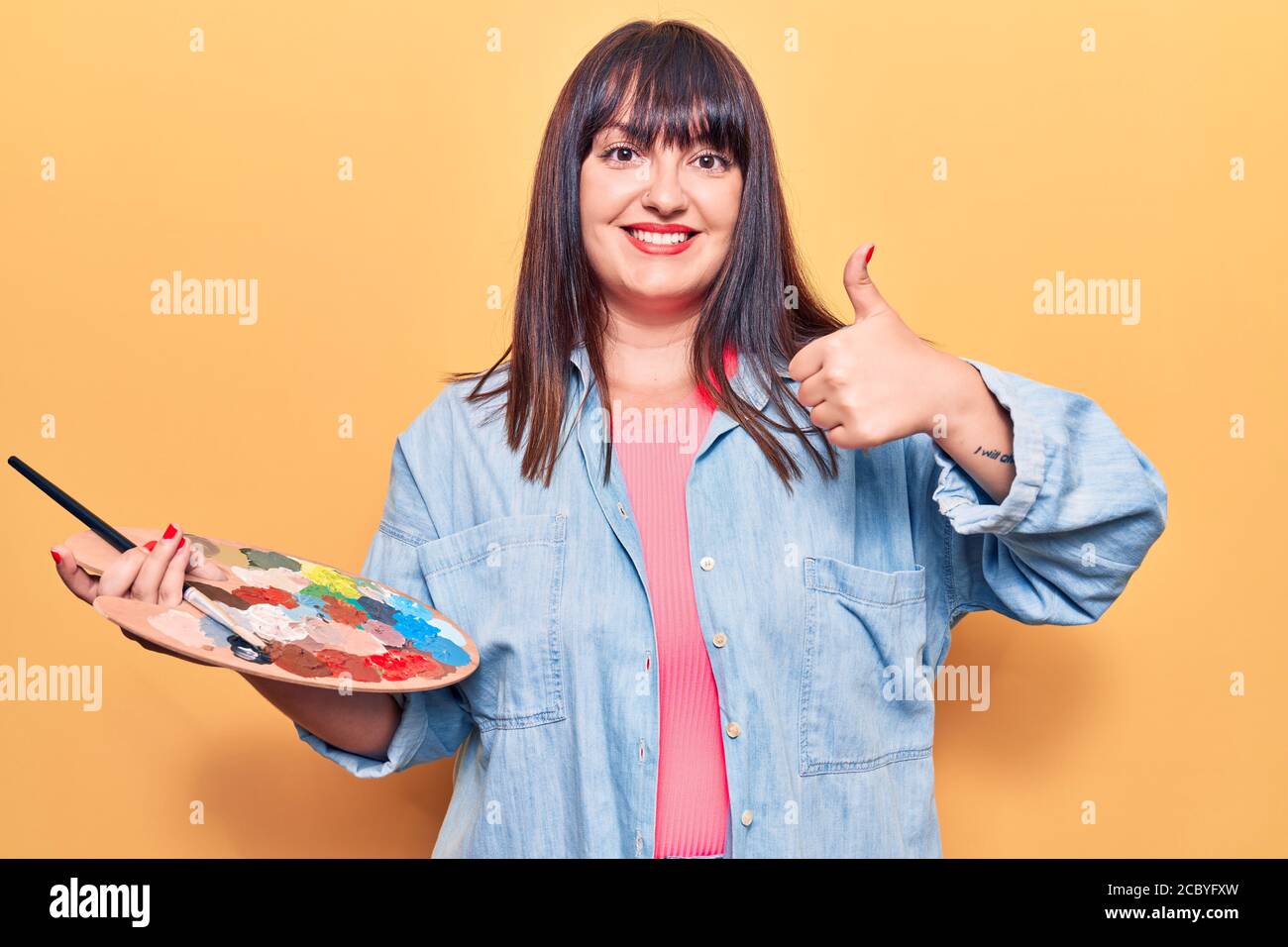 Young plus size woman holding paintbrush and palette smiling happy and ...