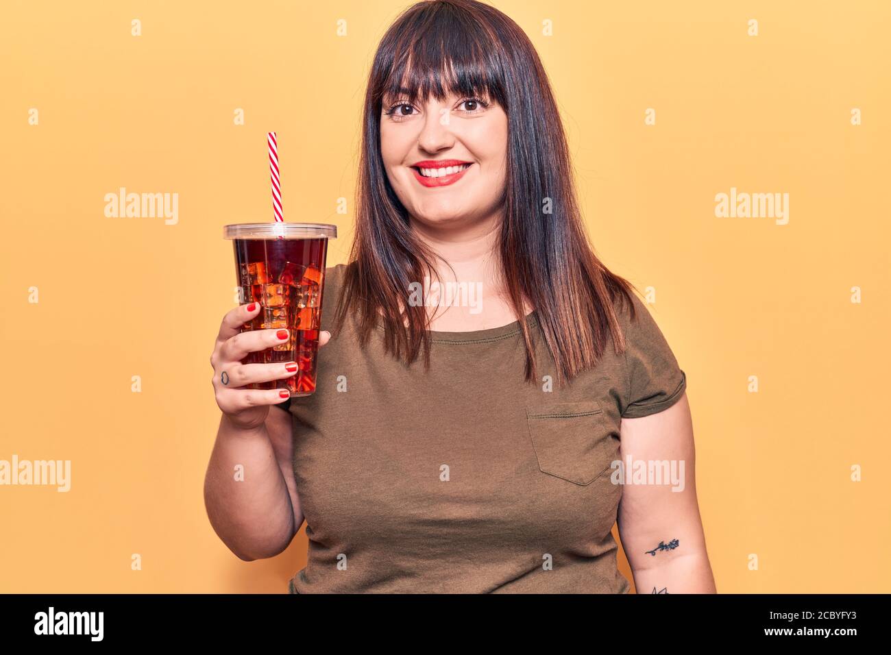 Young plus size woman drinking glass of cola beverage looking positive ...