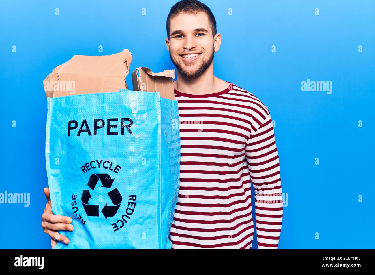 Young handsome man recycling paper looking positive and happy standing ...
