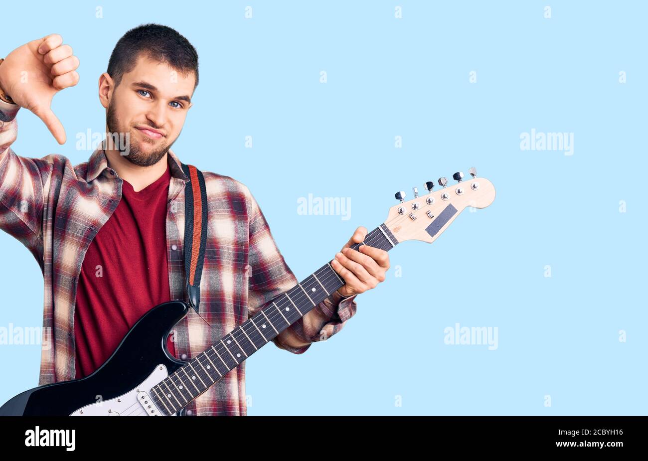 Young handsome man playing electric guitar with angry face, negative ...