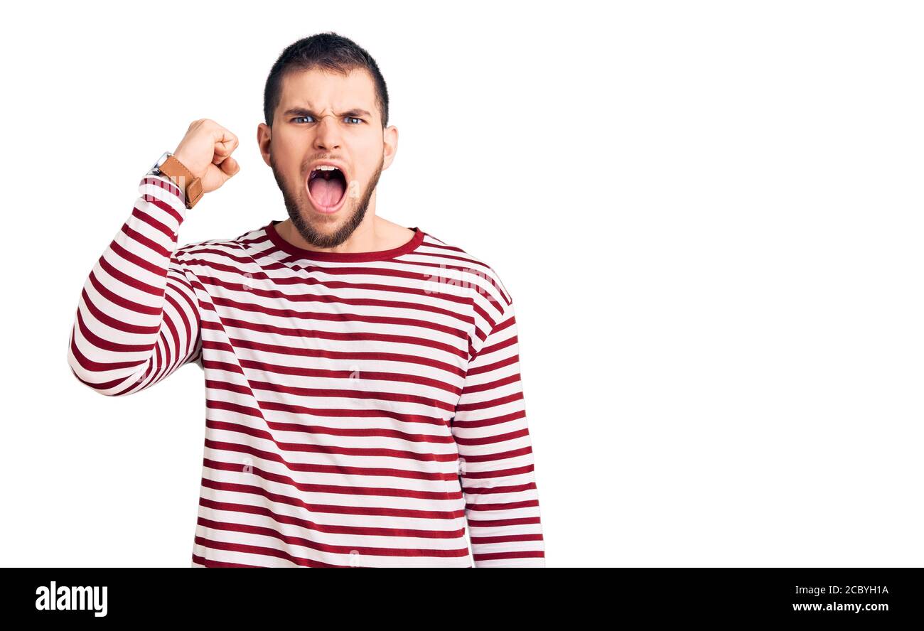 Young handsome man wearing striped sweater angry and mad raising fist ...
