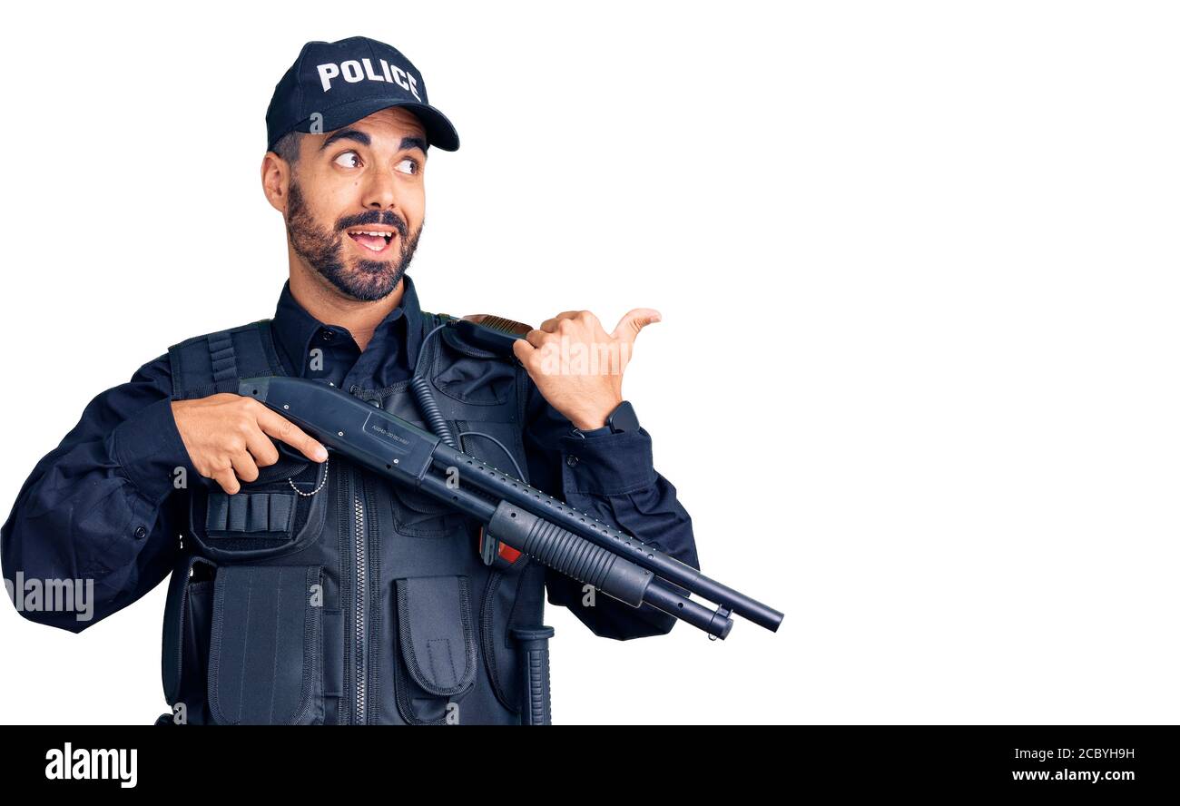 Young hispanic man wearing police uniform holding shotgun pointing ...