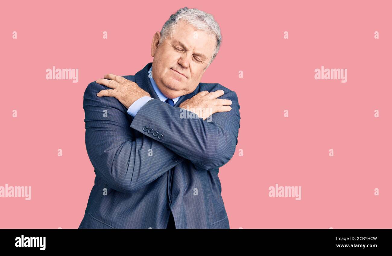 Senior grey-haired man wearing business jacket hugging oneself happy ...