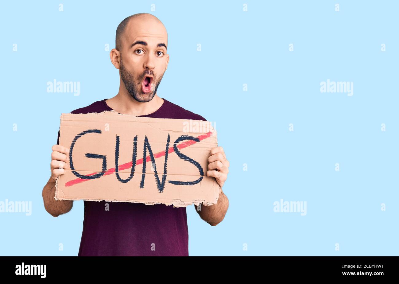 Young handsome man holding prohibited guns banner scared and amazed ...
