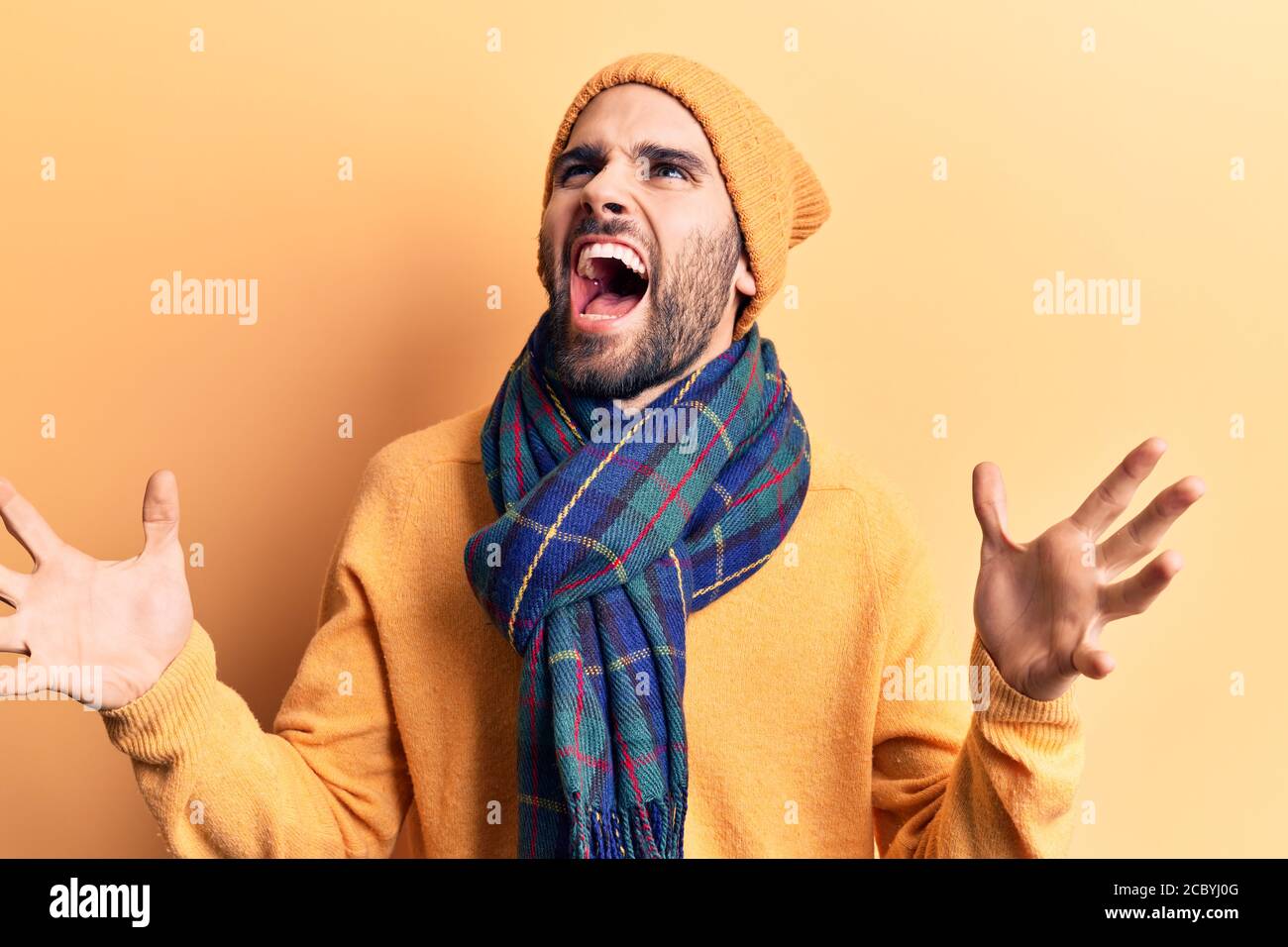Young handsome man with beard wearing wool cap and scarf crazy and mad ...