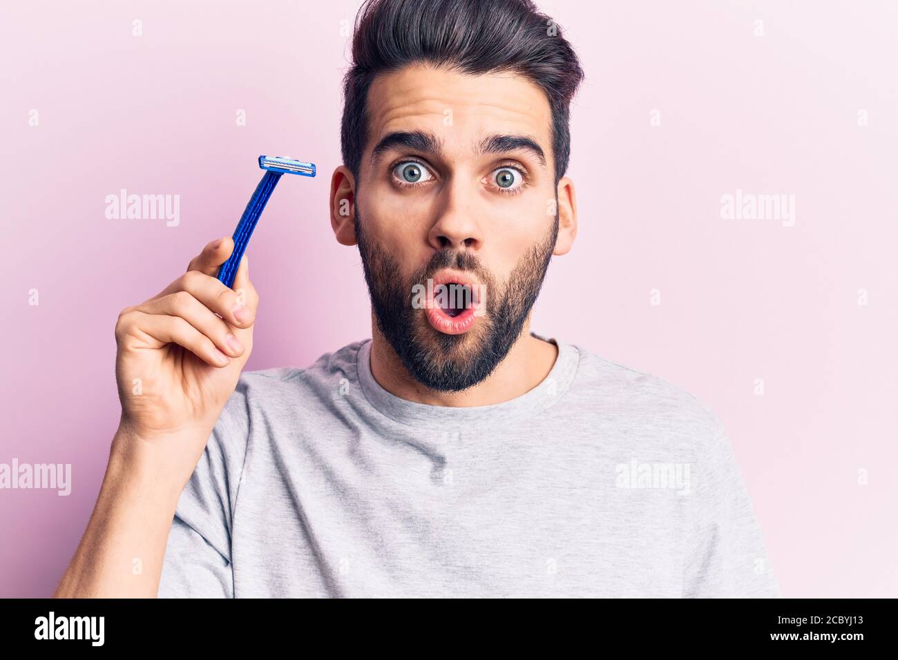 Young handsome man with beard holding razor scared and amazed with open ...