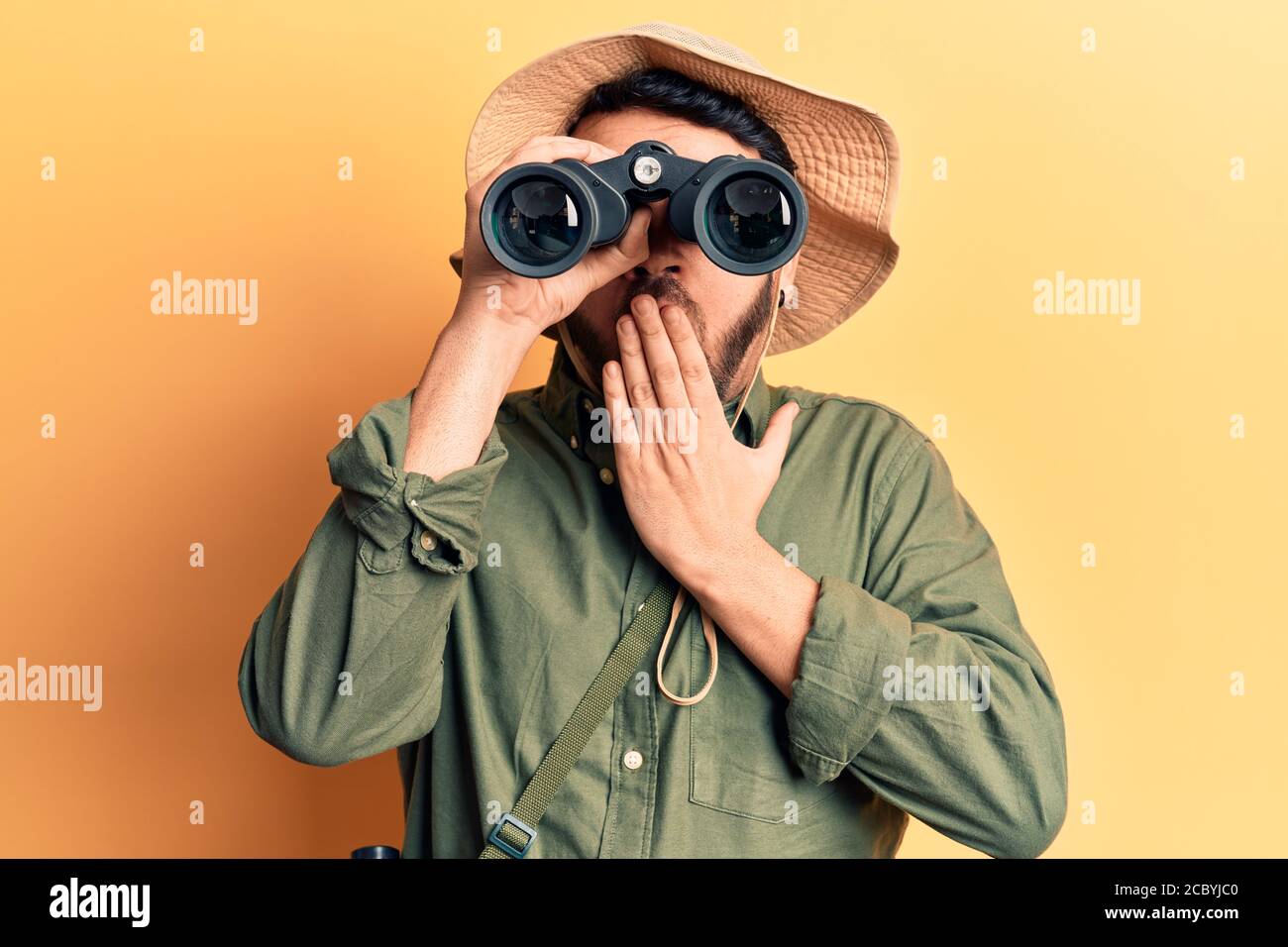 Young hispanic man wearing explorer hat holding binoculars covering ...