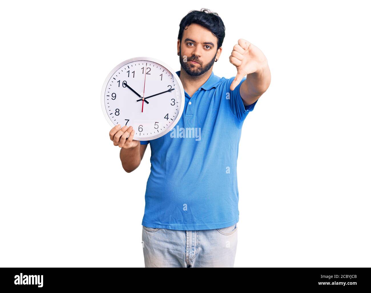 Young hispanic man holding big clock with angry face, negative sign ...