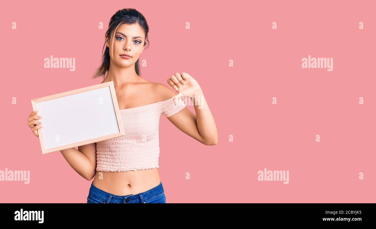 Young beautiful woman holding empty white chalkboard with angry face ...