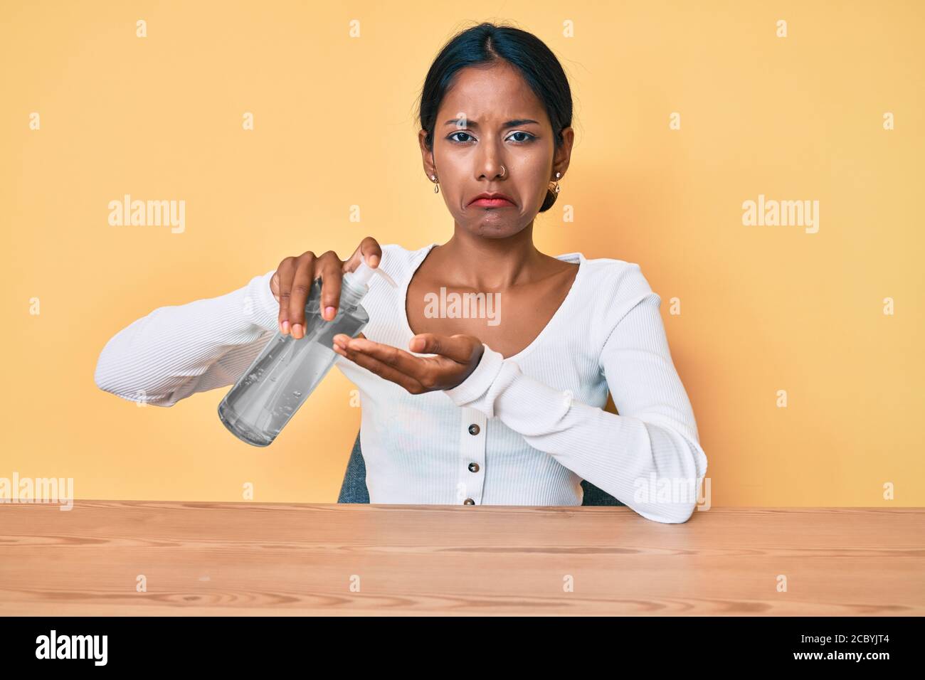 Young indian girl sitting on the table cleaning hand using sanitizer ...