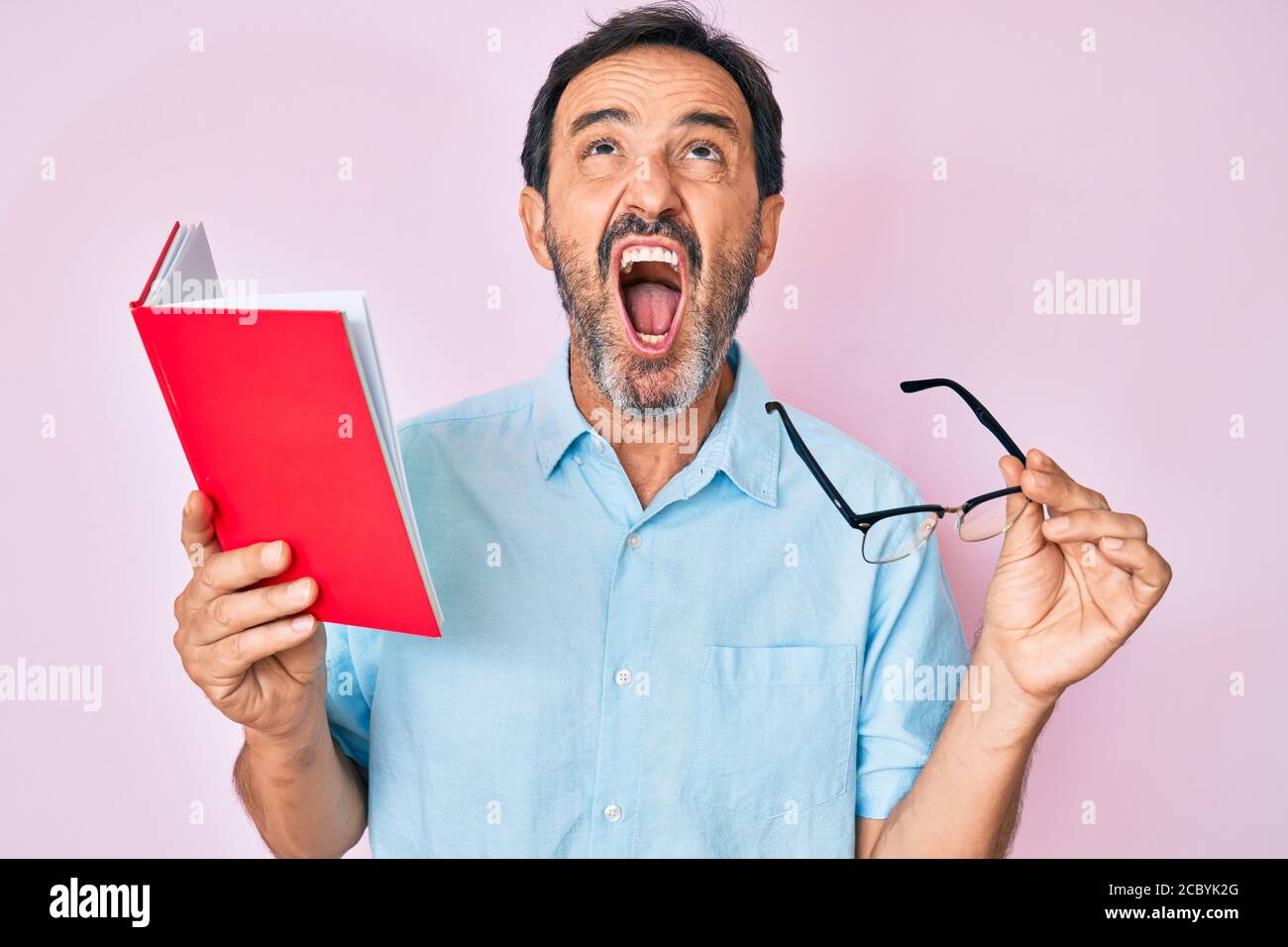 Middle age hispanic man reading book holding glasses angry and mad ...