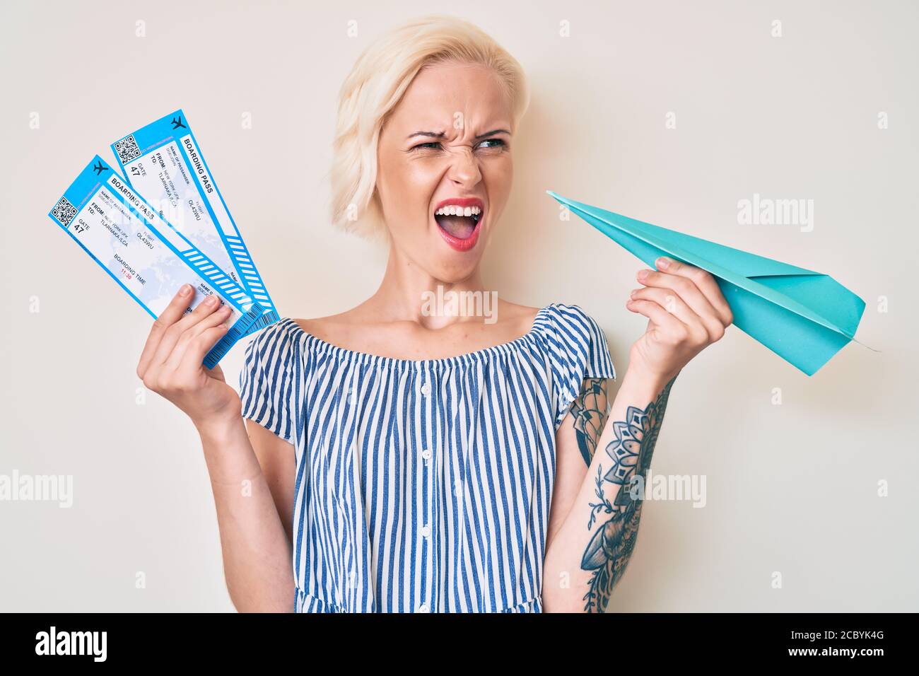 Young blonde woman with tattoo holding paper airplane and boarding pass ...