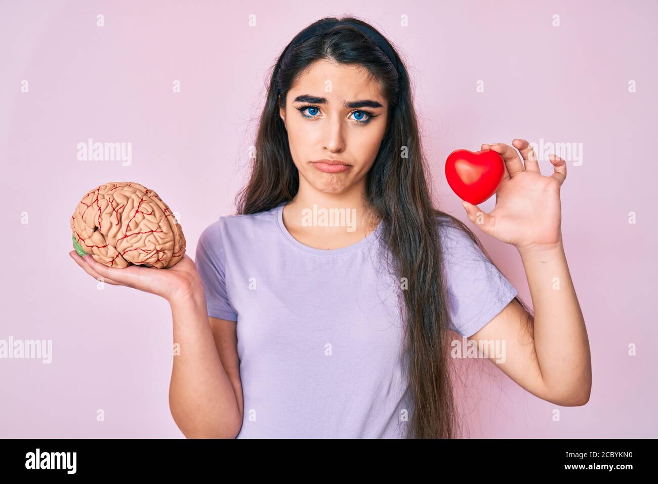 Brunette teenager girl holding brain and heart depressed and worry for ...