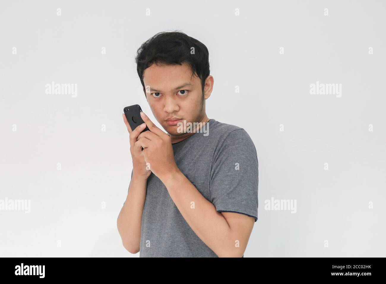 Asian man serious face and sharp looking with hiding the phone gesture ...
