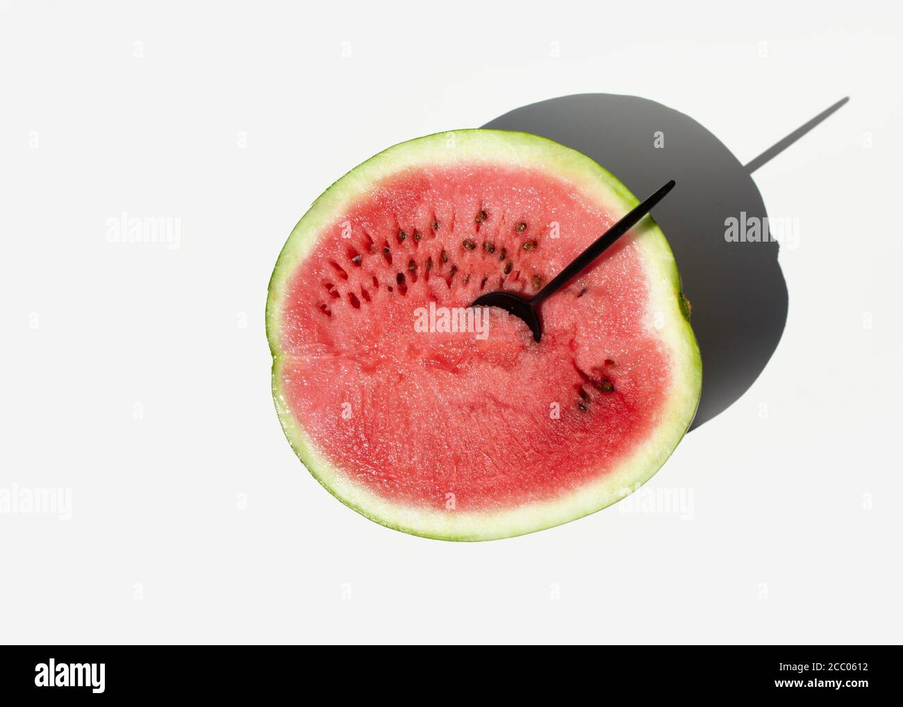 A tablespoon inserted in a half ripe watermelon on white background ...