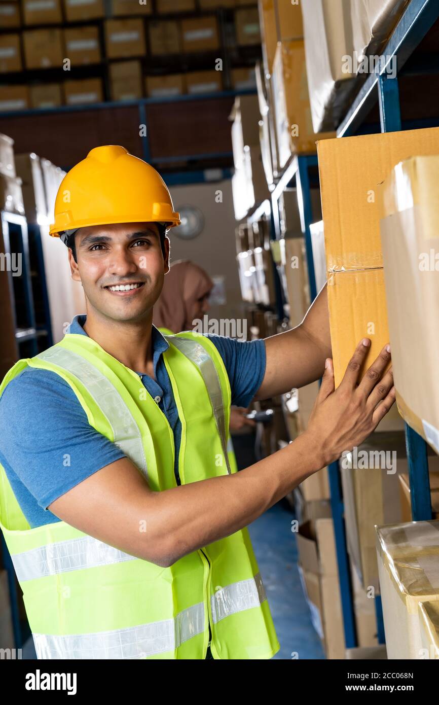Portrait of Indian warehouse worker put cardboard box in to shelf with ...