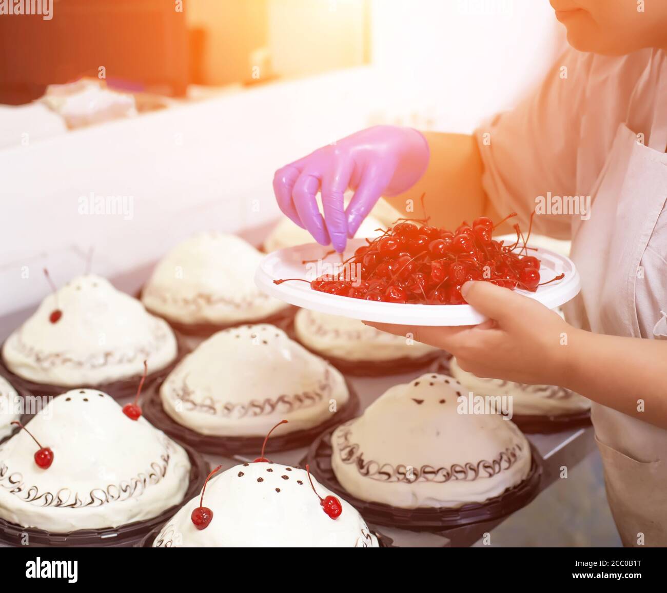 A chef decorates cakes in a confectionery factory with fresh cherry ...