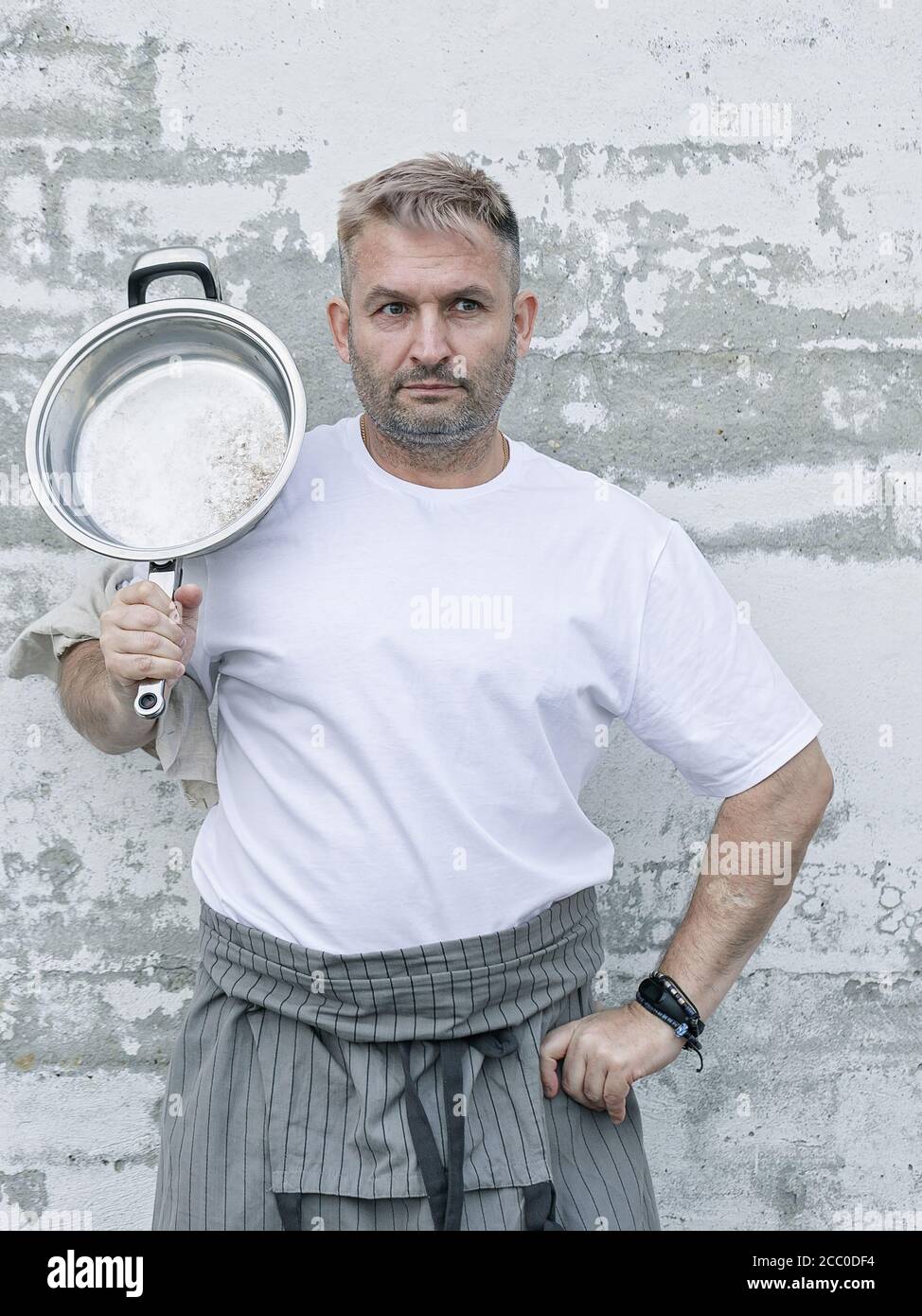 Stylish chef in a white T-shirt and a striped apron with a frying pan ...