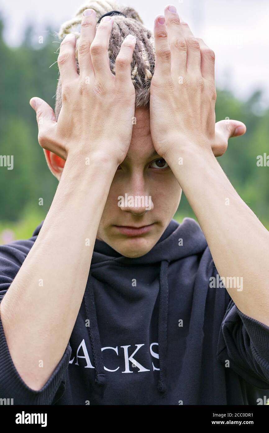 Portrait of a young guy with dreadlocks. Depression emotion. Covers his ...