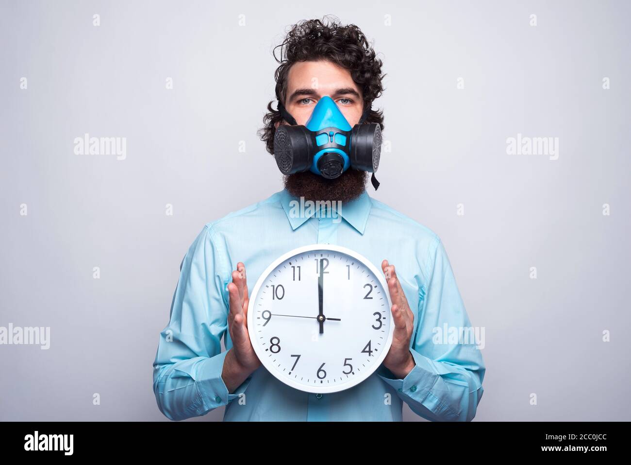 Photo of young man in casual wearing respirator and holding white clock ...