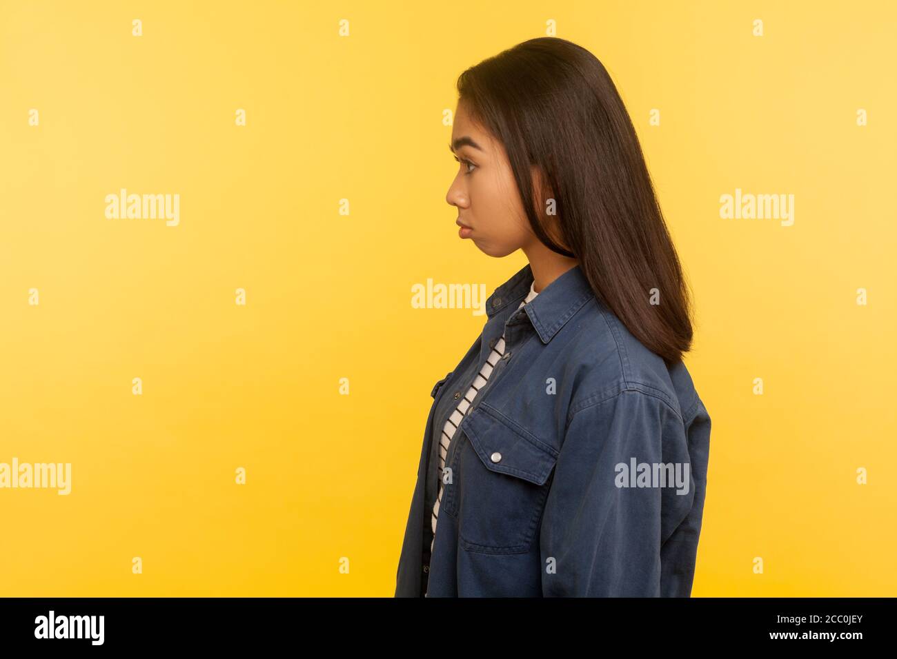 Side view of upset girl in denim shirt standing with unhappy gloomy ...