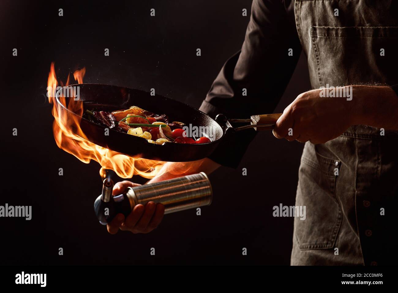 Chef cooks with fire in a pan shrimp with vegetables. On a black ...