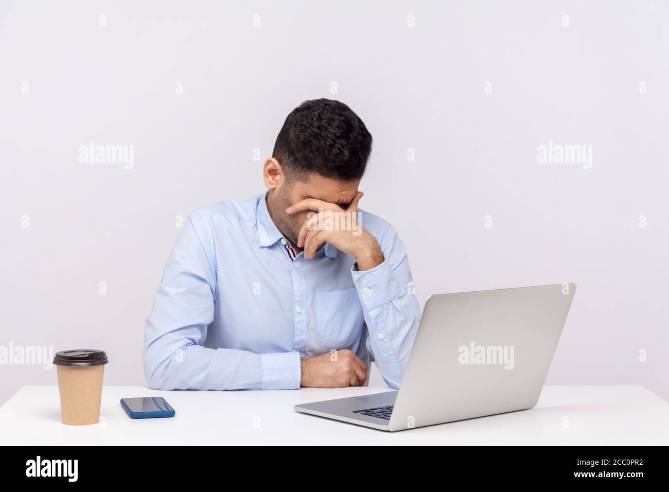 Upset man employee sitting office workplace with laptop on desk, bowing ...