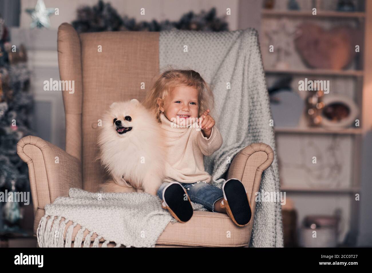 Smiling baby girl 3-4 year old wth spitz puppy sitting in cozy chair in ...