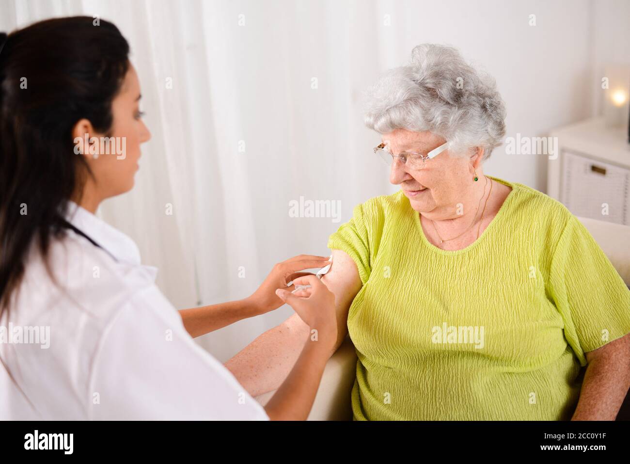 cheerful young nurse giving an injection to a elderly senior woman at ...