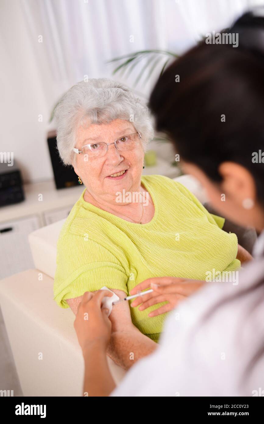 cheerful young nurse giving an injection to a elderly senior woman at ...