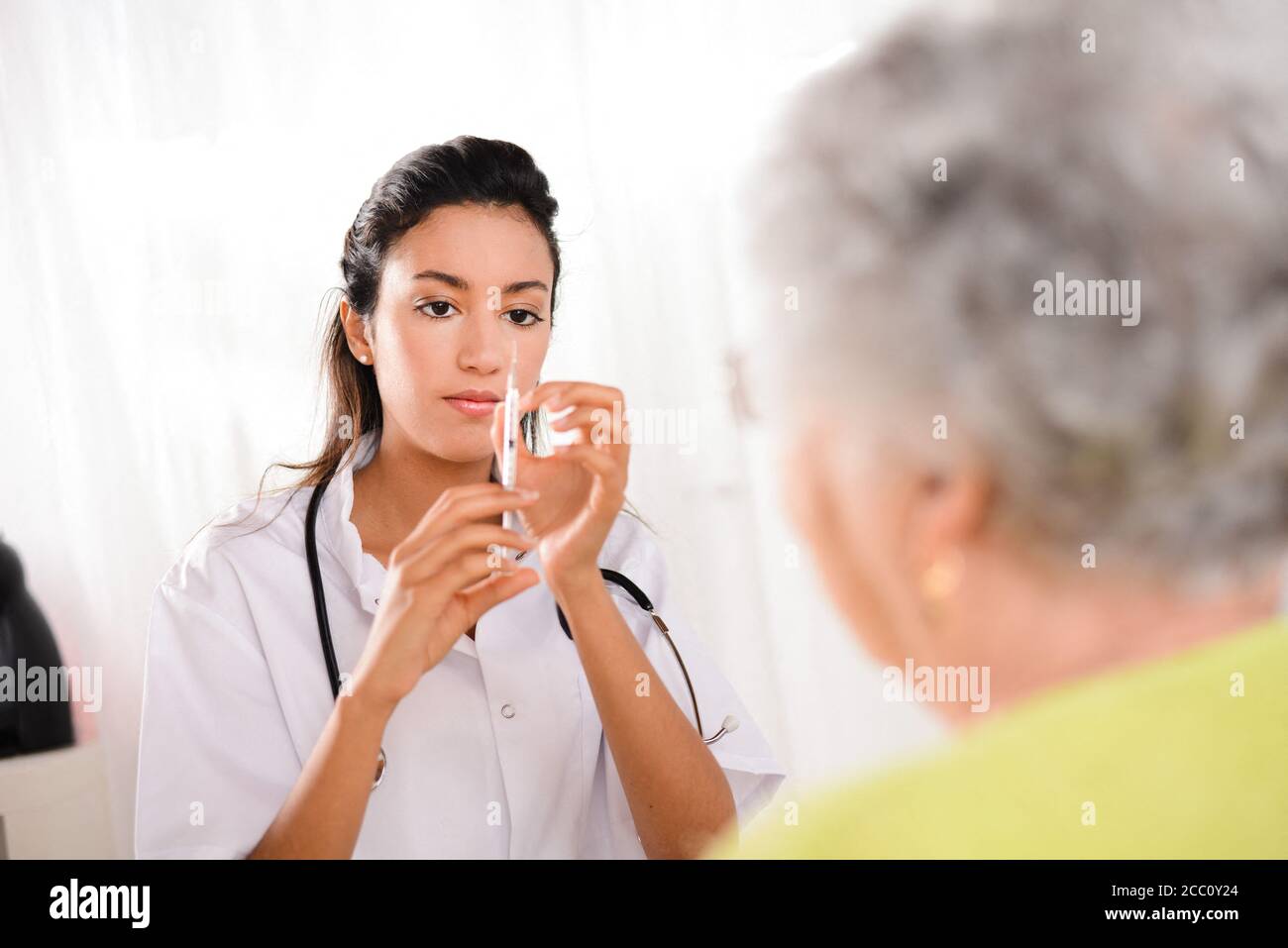 cheerful young nurse giving injection to a elderly senior woman at home ...