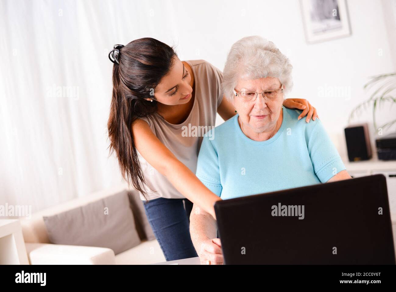 cheerful young woman helping an elderly senior person using laptop ...