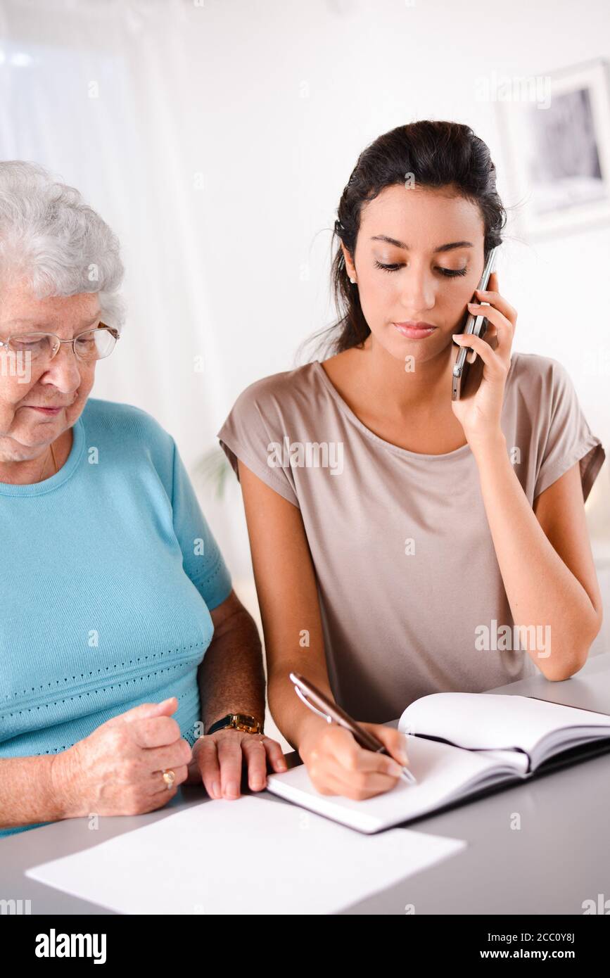 cheerful young woman helping an old senior person doing paperwork and ...