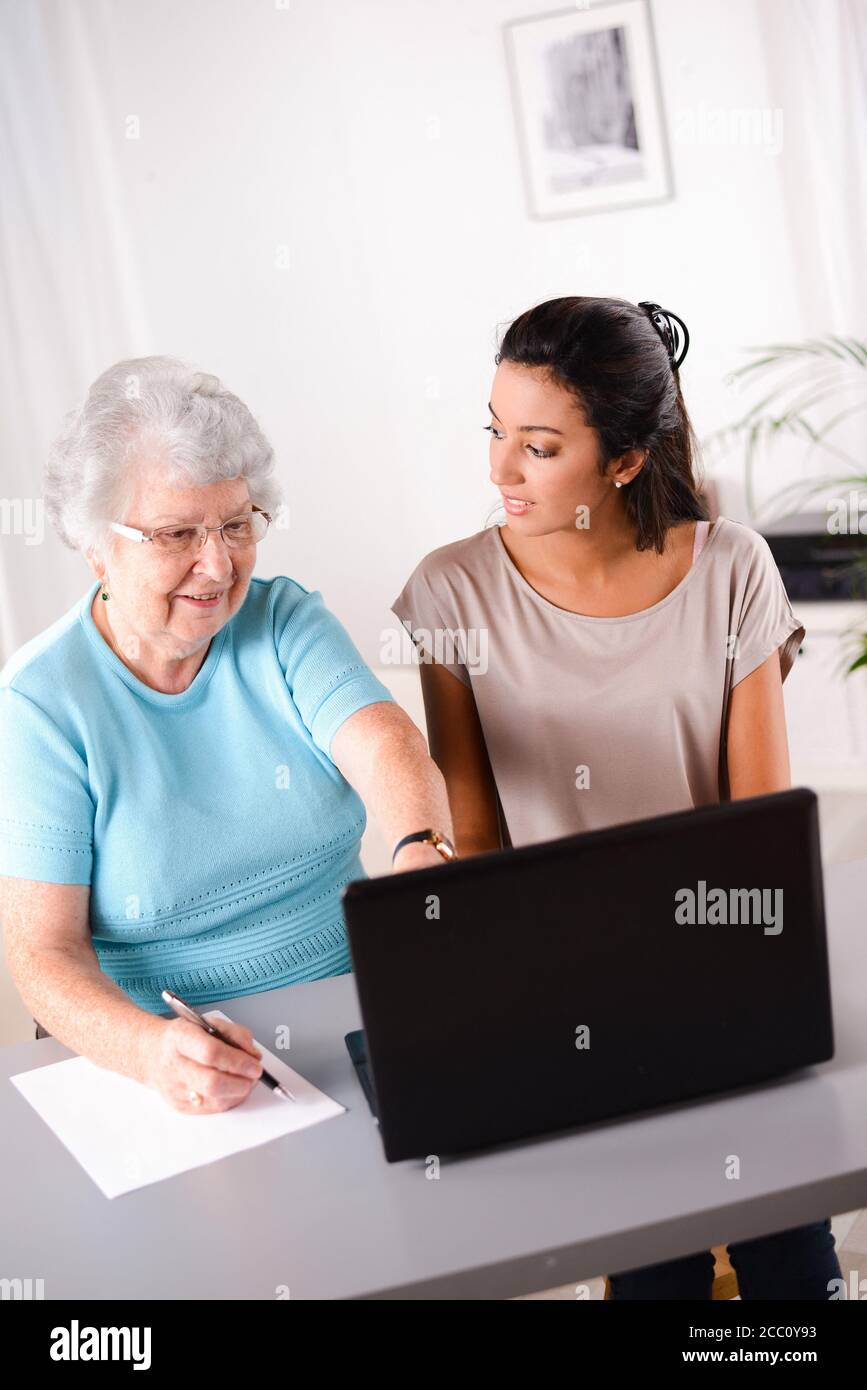 cheerful young woman helping an elderly senior person using laptop ...