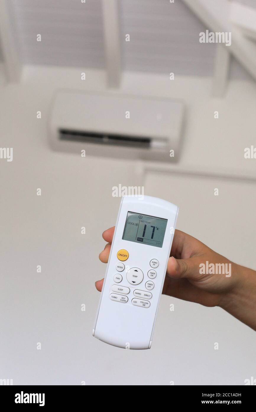 Young woman using a remote control of wall-mounted air conditioner ...