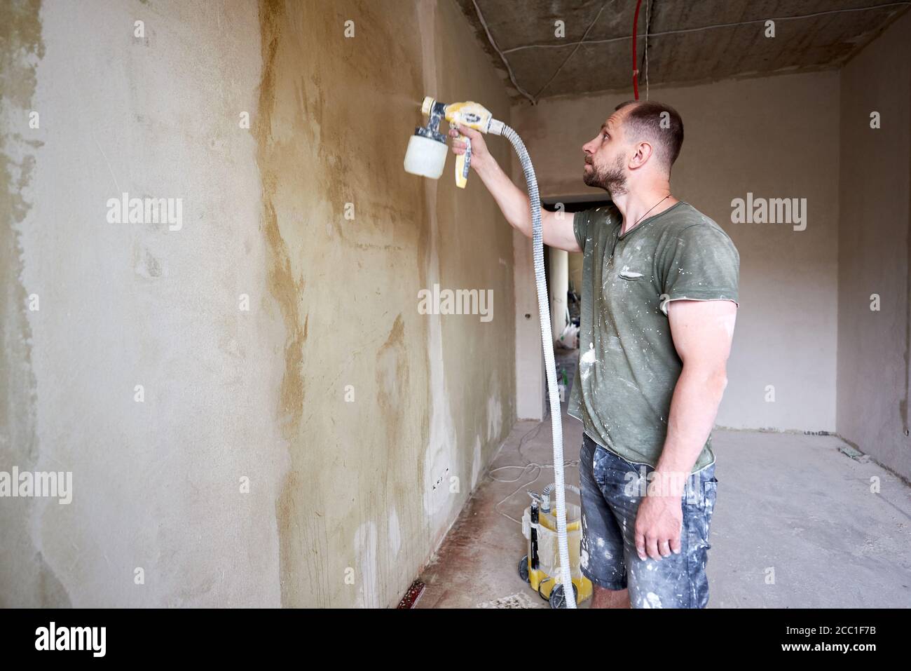 Side view of male builder is painting with airbrush wall, house ...