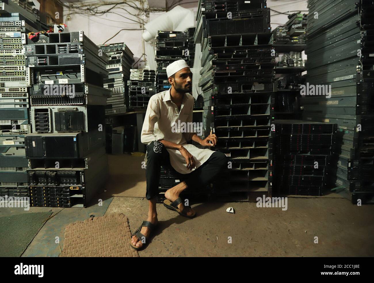 A man sits in front of electronic waste or e-waste from computers at a ...