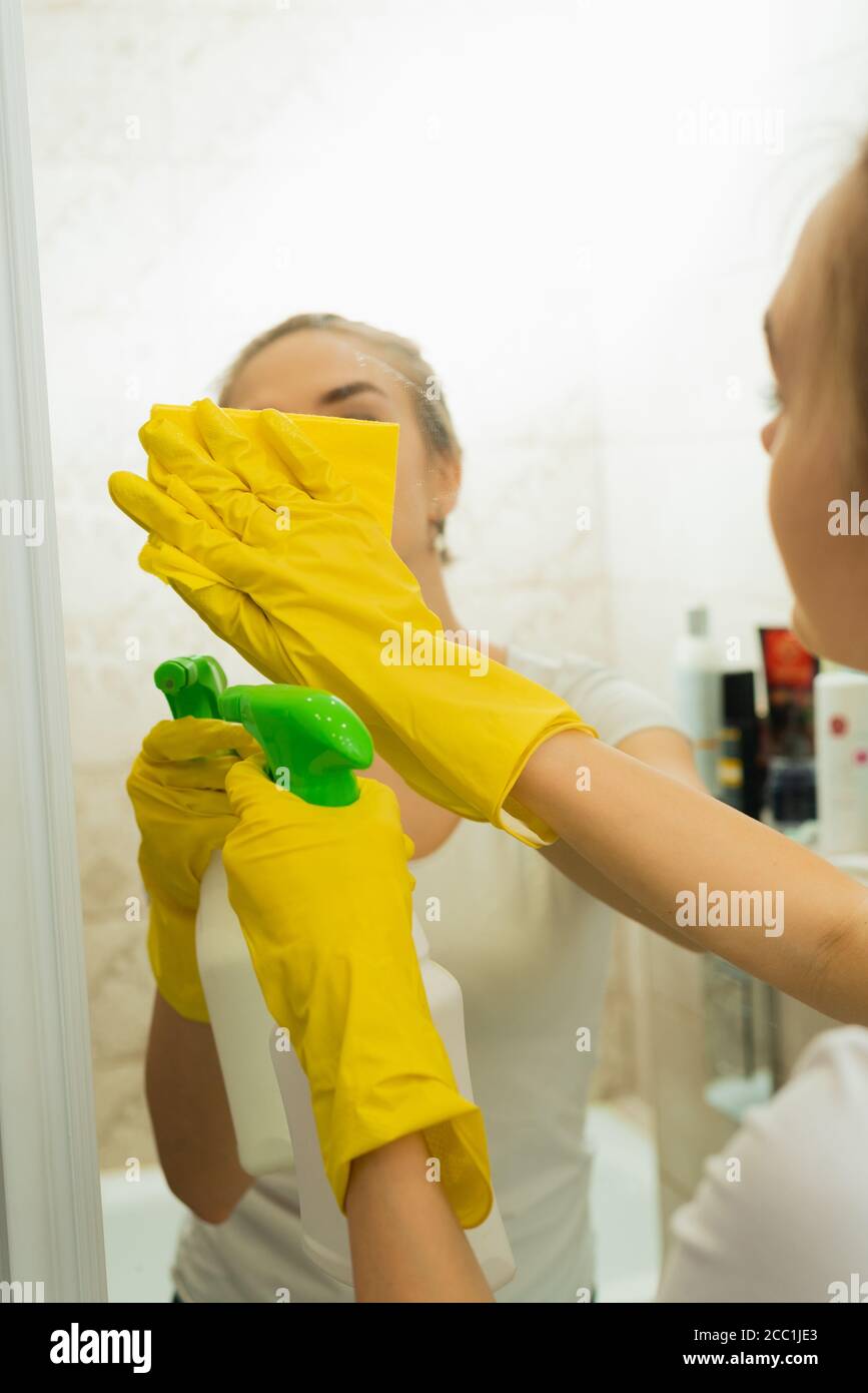 A woman is washing a mirror in yellow gloves. A young woman is cleaning ...