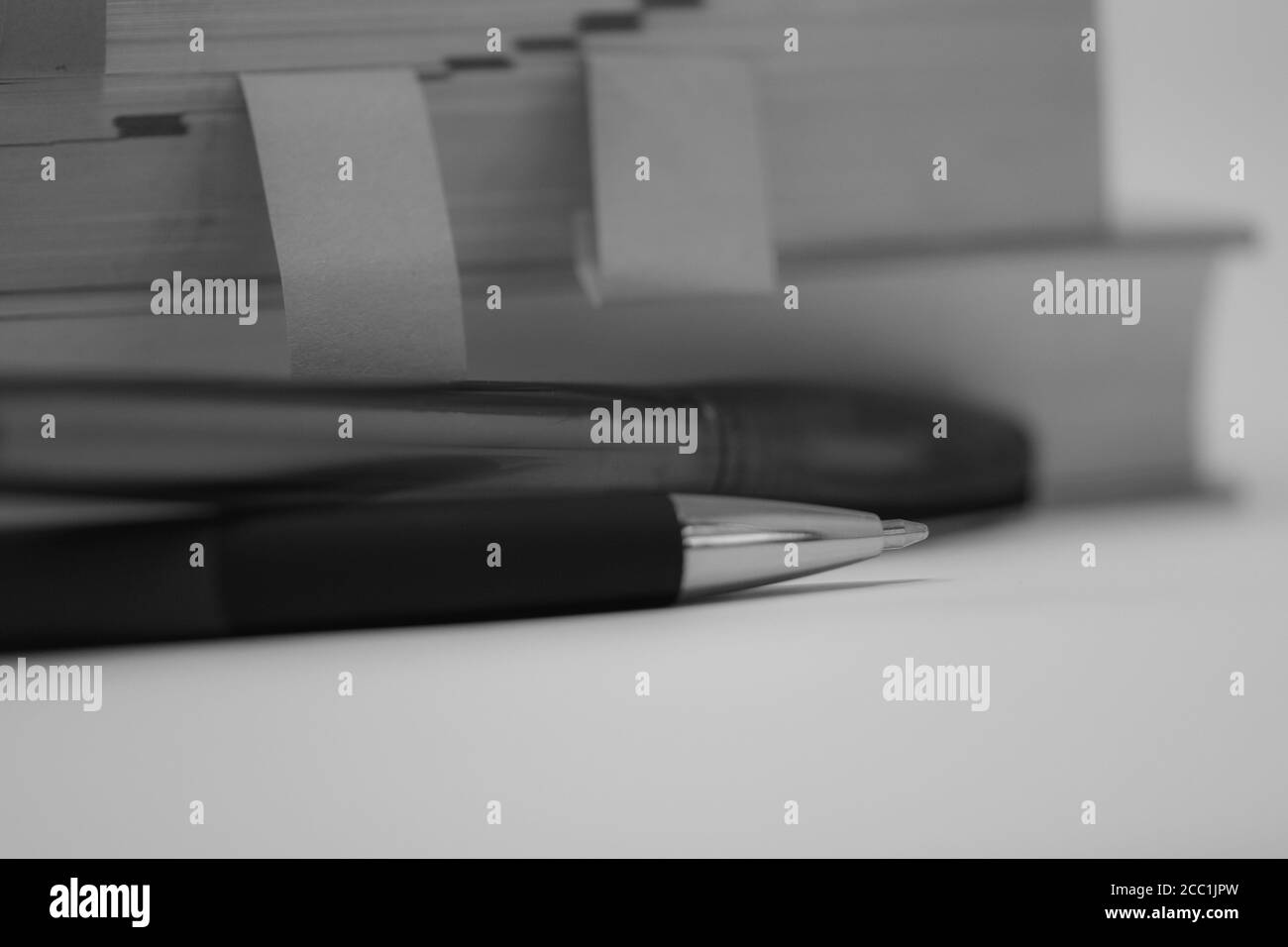 Greyscale shot of pens by some books on a table Stock Photo - Alamy